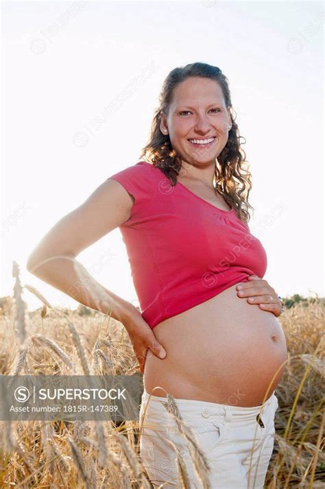 Germany, Brandenburg, young pregnant woman standing in cornfield ...